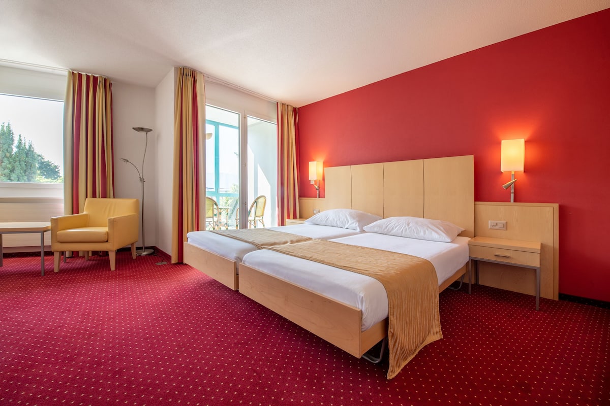 Quarto de hotel com uma cama grande, duas mesas de cabeceira, uma escrivaninha e uma cadeira.