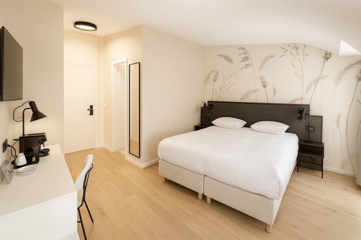 Quarto com cama, mesas de cabeceira, escrivaninha com cadeira e espelho.