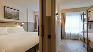 Quarto de hotel com uma cama, uma mesa, uma cadeira, uma janela com cortinas e uma beliche.