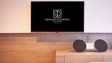 Quarto de hotel moderno com televisão de tela plana na parede, exibindo o logotipo do Grand Plaza Hotel.