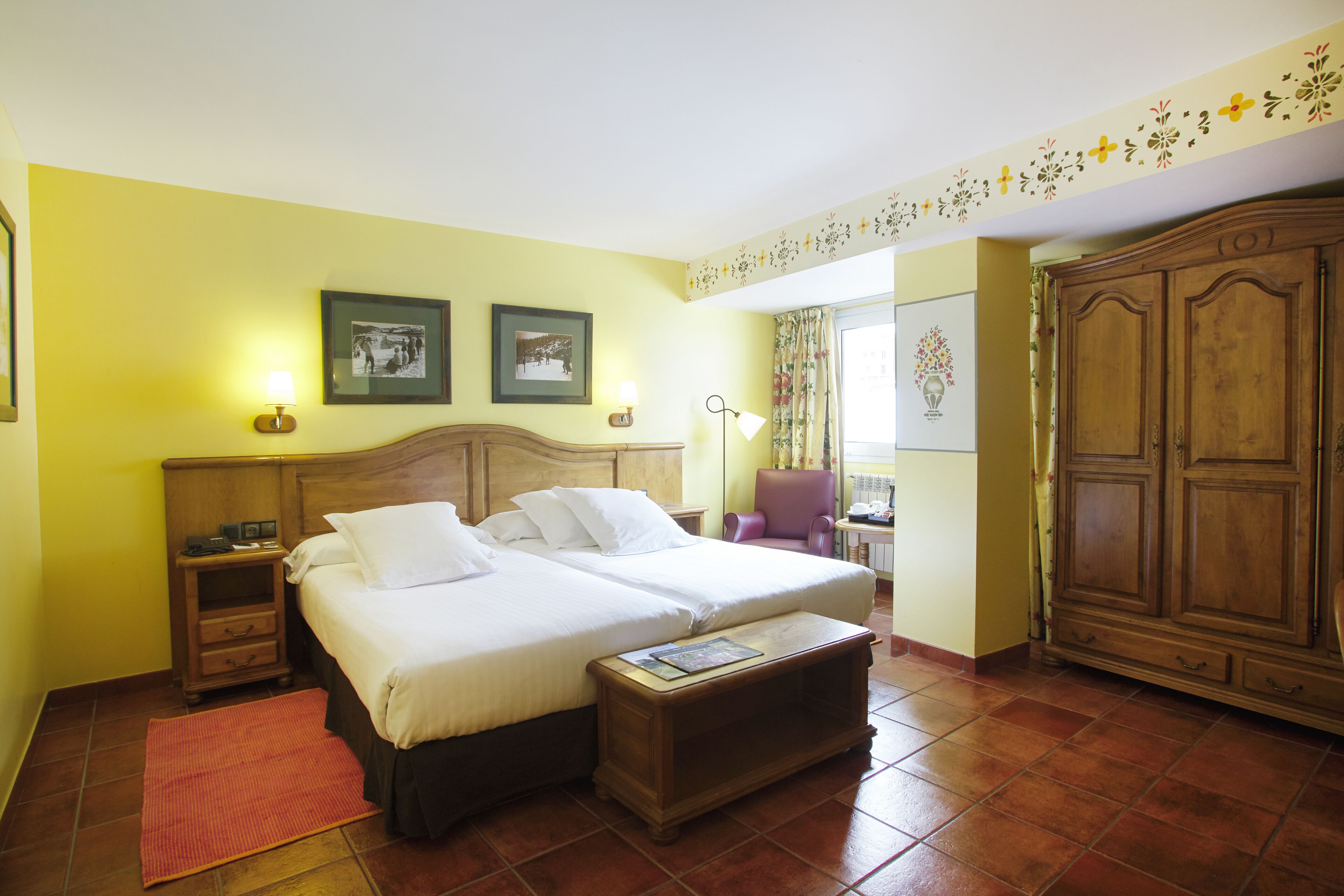 Quarto de hotel com cama de casal, mesa de cabeceira de madeira, uma cadeira, guarda-roupa e tapete vermelho.