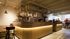 Um restaurante moderno com balcão e área de bar em madeira, espaço de estar com mesa e cadeiras, e cozinha ao fundo.
