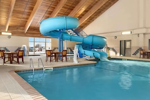 Piscina interna com escorregador azul e área de estar com cadeiras e mesas.