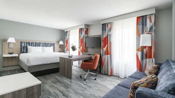 Quarto de hotel com cama, escrivaninha, cadeira de escritório, sofá e televisão.