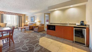 Quarto de hotel com área de refeições, sofá, máquina de café e micro-ondas.