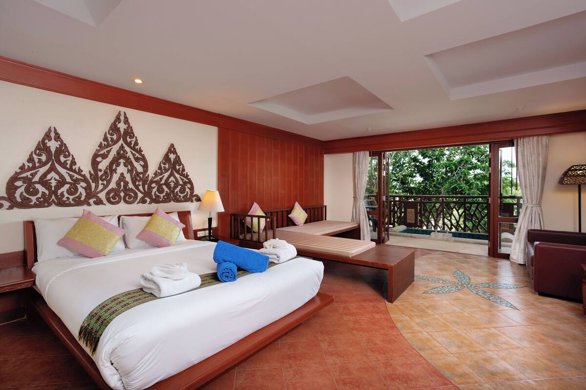 Quarto de hotel com uma cama grande, um banco de madeira, um sofá e vista para o exterior.