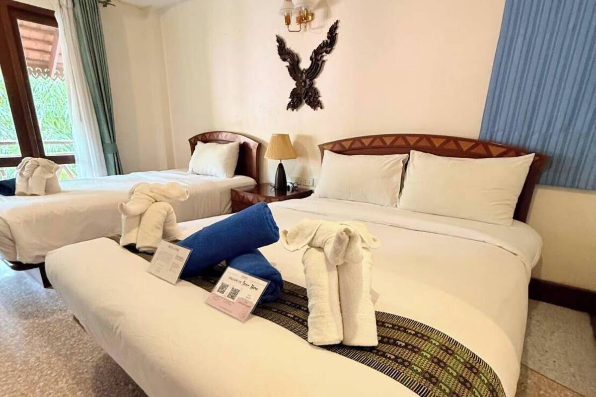 Quarto de hotel com duas camas, um candelabro e vista para o verde lá fora.