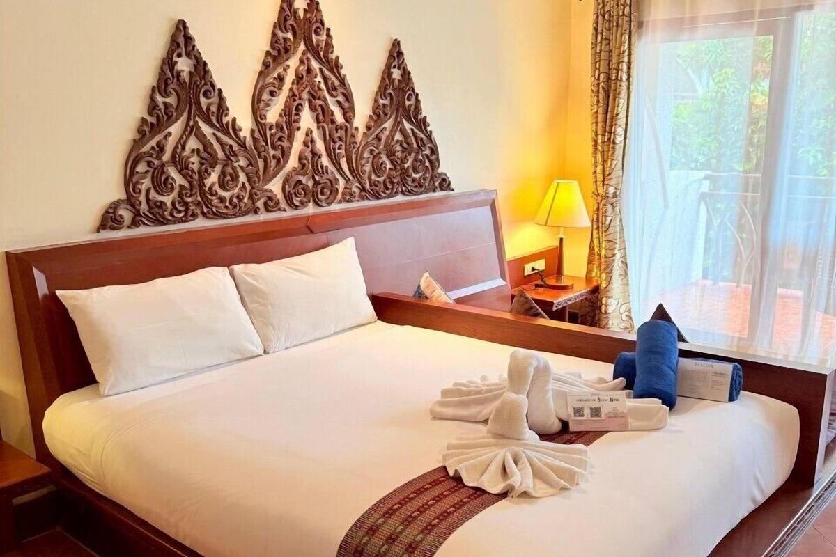 Uma cama grande com lençóis brancos, cabeceira de madeira e arte decorativa na parede.
