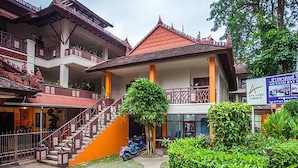Um edifício tradicional com uma escadaria que leva a uma varanda, rodeado por vegetação e uma scooter estacionada.