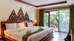 Quarto de hotel com uma cama grande, um objeto decorativo na parede, varanda com vista para áreas verdes e uma porta de correr.