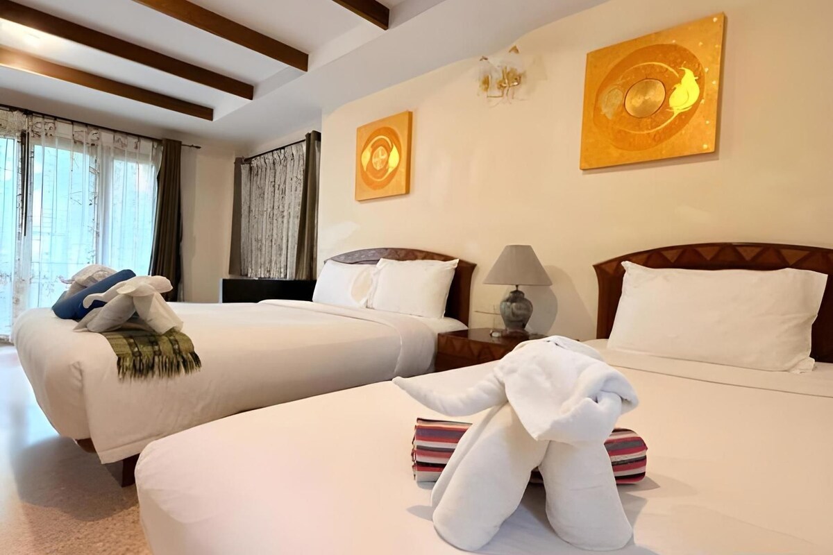 Quarto de hotel com duas camas, mesa de cabeceira com abajur e obras de arte nas paredes.