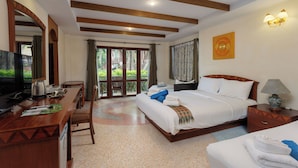 Quarto de hotel com cama, escrivaninha, televisão e varanda com cortinas.
