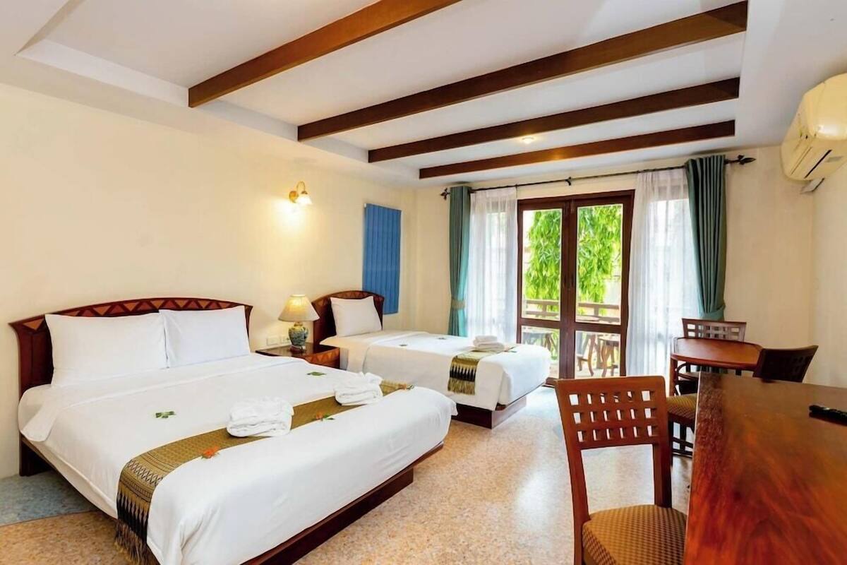 Quarto de hotel com duas camas, teto de madeira, mesa de jantar e vista para o verde lá fora.