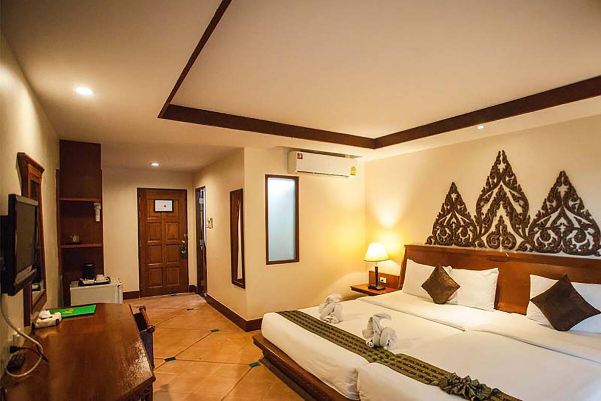 Quarto de hotel com cama, mesa de cabeceira, abajur, parede decorativa e televisão.