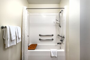 Uma banheira branca com um tabuleiro de madeira, duas barras de apoio metálicas e um porta-toalhas com toalhas.