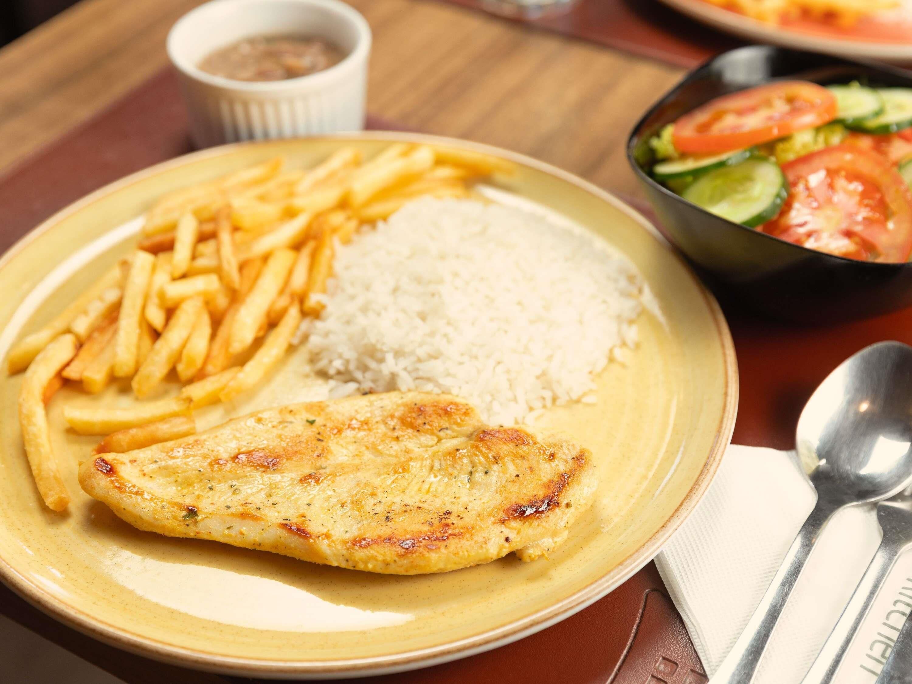 Um prato com peito de frango grelhado, batatas fritas e arroz branco.