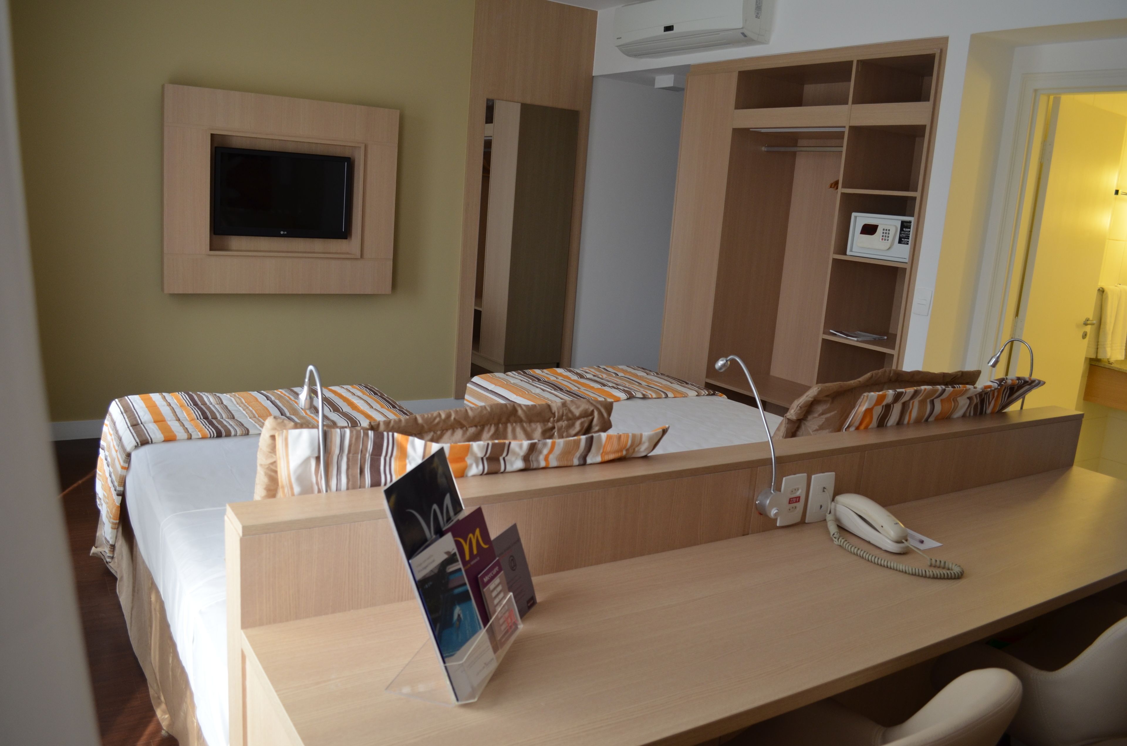 Quarto de hotel com uma cama, uma escrivaninha com telefone e suporte para revistas, micro-ondas e televisão na parede.