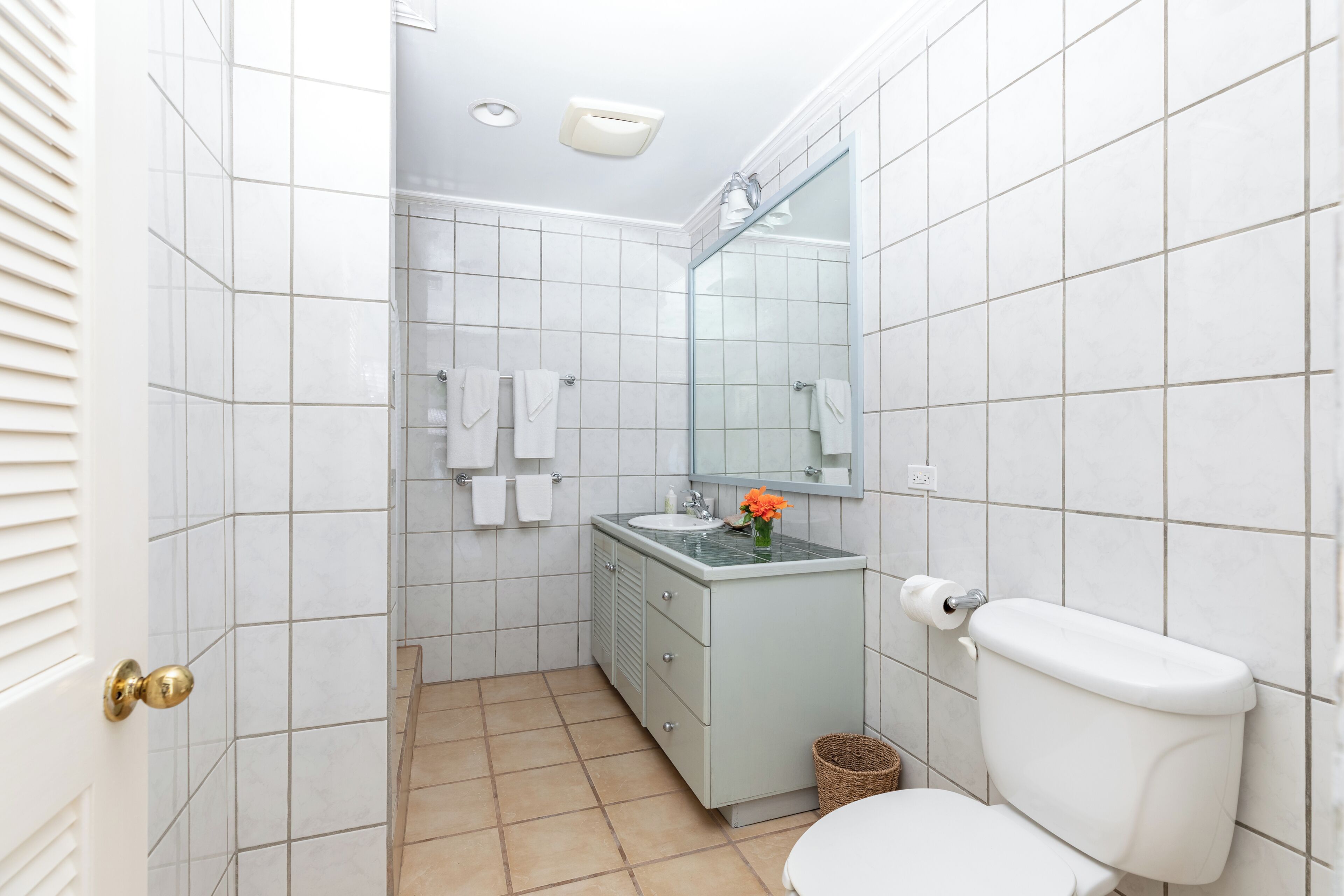 Um banheiro com azulejos brancos, pia, vaso sanitário, espelho e chuveiro.