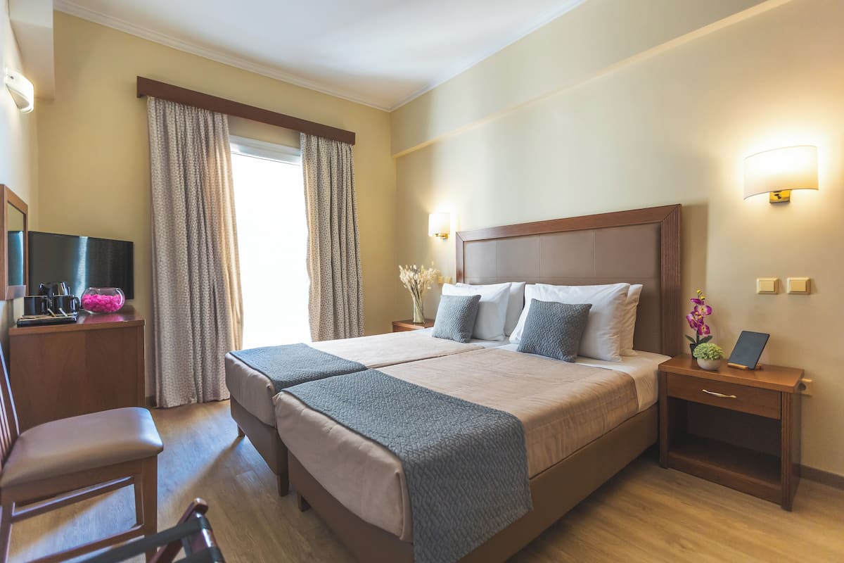 Quarto de hotel com cama grande, duas mesas de cabeceira, televisão e janela com cortinas.