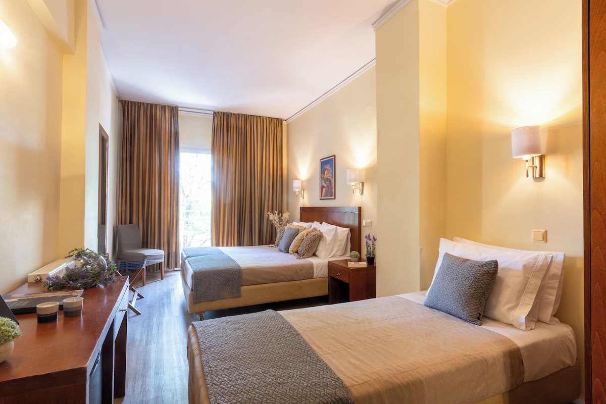 Quarto de hotel com duas camas, uma mesa com um laptop, uma cadeira e uma janela com cortinas.