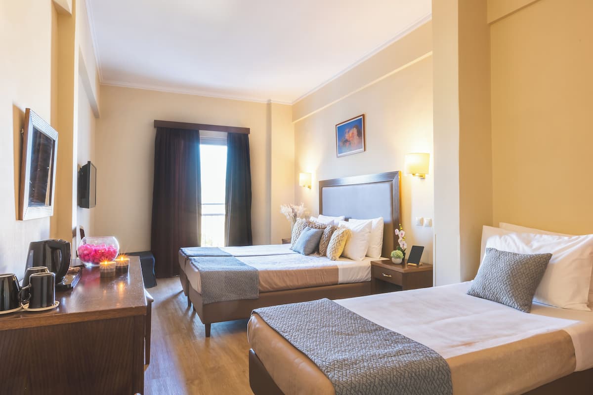 Quarto de hotel com duas camas, uma escrivaninha com cafeteira e vista para o exterior.