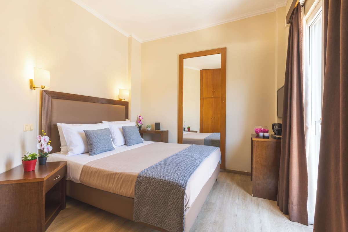 Quarto de hotel com uma cama grande, mesas de cabeceira, um espelho, um guarda-roupa e uma televisão.