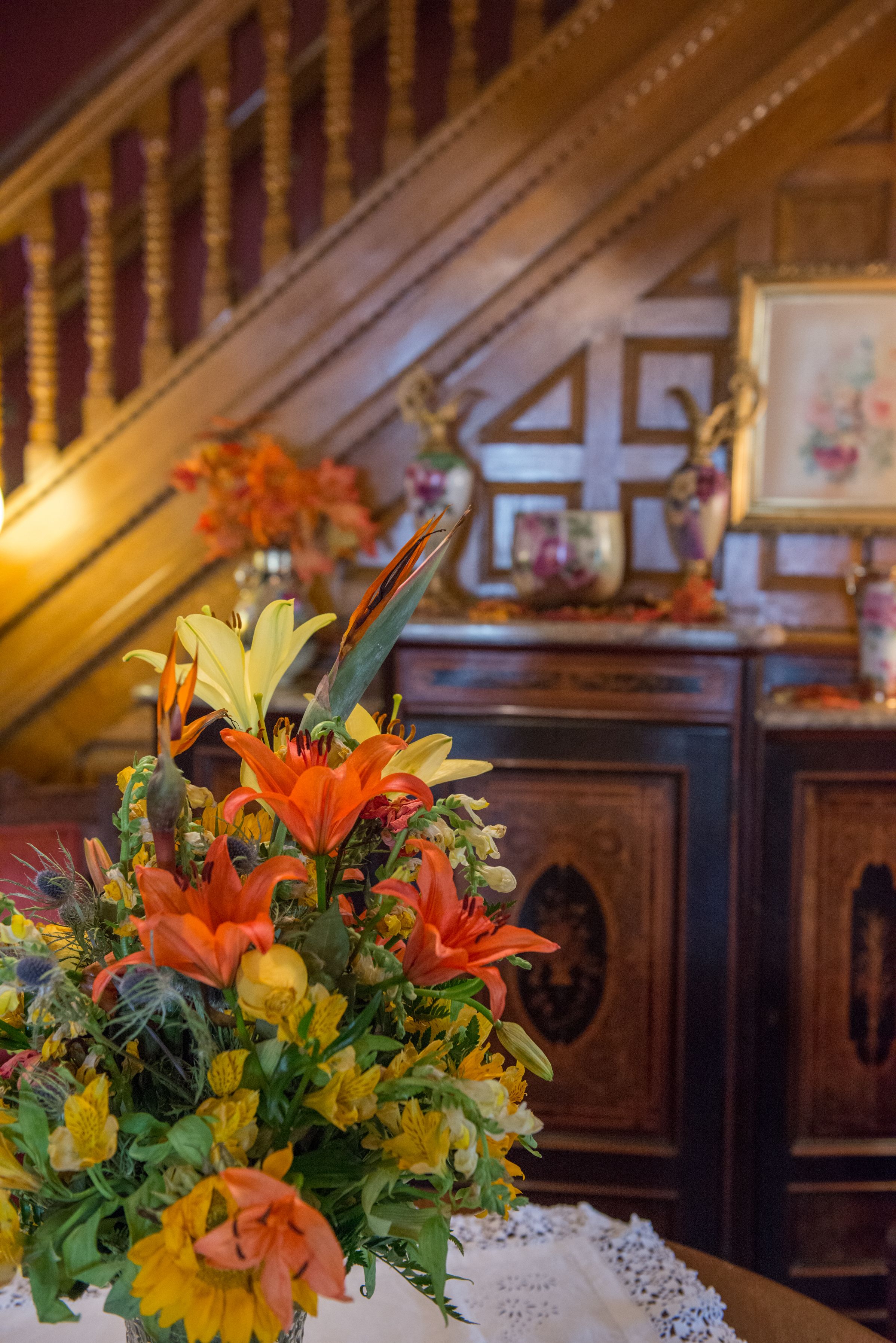 Um quarto com uma escada de madeira, um arranjo floral sobre uma mesa e um armário com objetos decorativos.