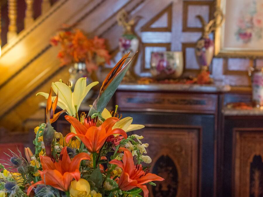 Um quarto com uma escada de madeira, um arranjo floral sobre uma mesa e um armário com objetos decorativos.