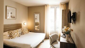 Quarto de hotel com cama, mesa de cabeceira, cadeira, escrivaninha, televisão e janela com cortinas.