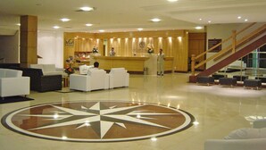 Um hall de hotel com balcão de recepção, área de estar e um grande emblema circular no chão.