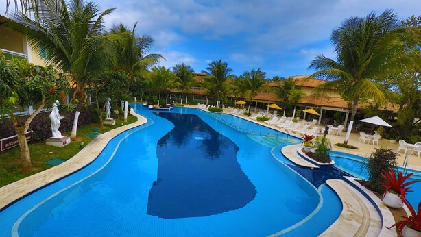 Uma piscina com design curvo, rodeada por palmeiras e espreguiçadeiras.