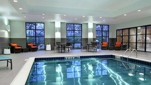 Piscina interior com água cristalina, rodeada por áreas de estar e grandes janelas.