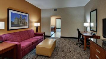 Quarto de hotel com sofá listrado, uma mesa pequena, escrivaninha com cadeira, televisão e um quadro na parede.