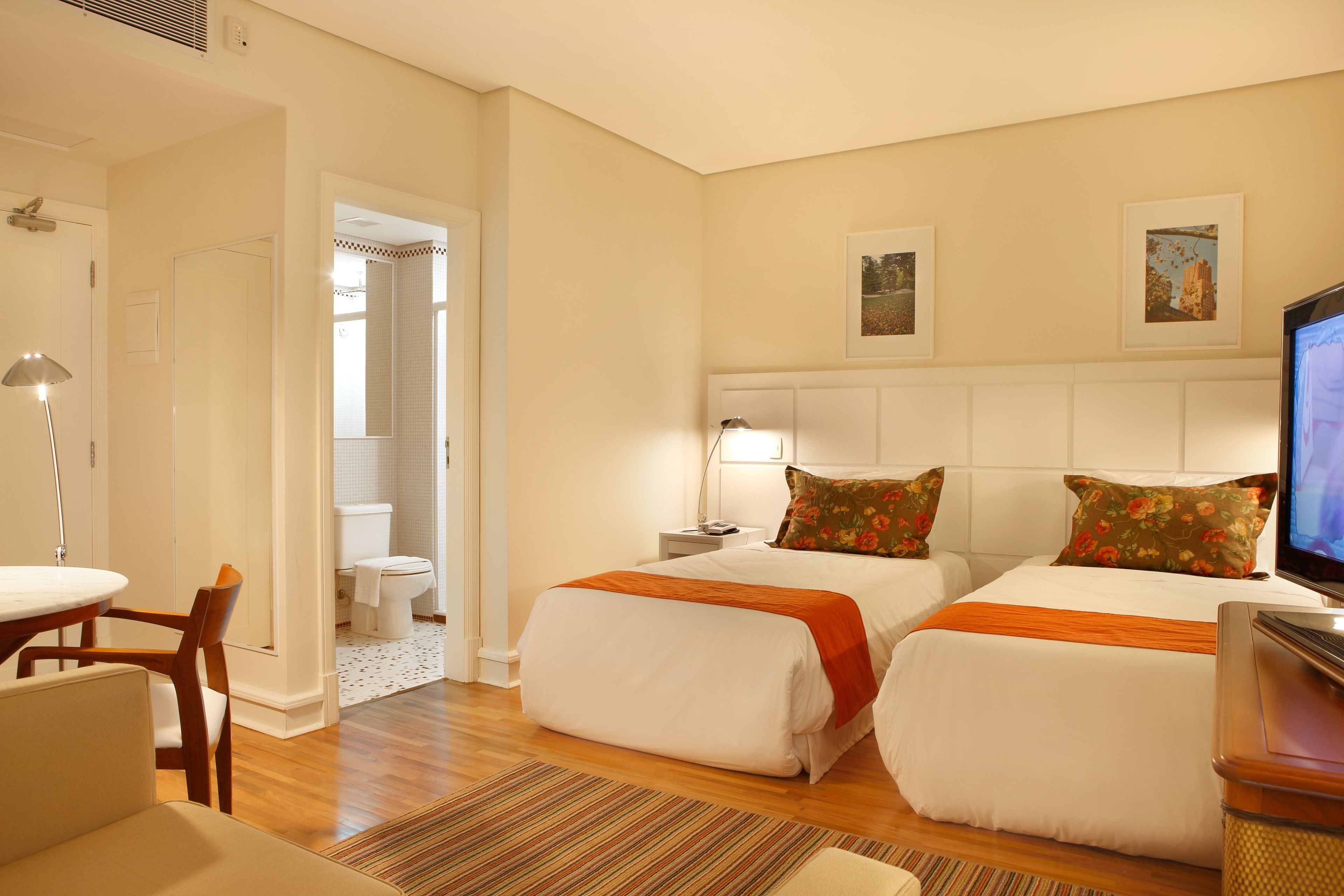 Quarto de hotel com duas camas, televisão, escrivaninha e banheiro.