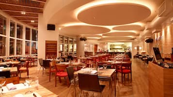 Um restaurante espaçoso com várias áreas de refeição, piso de madeira e um design moderno no teto.