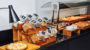 Buffet com diversos alimentos, incluindo pão, doces e acompanhamentos em potes.