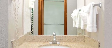 Um banheiro com pia de granito, um espelho, porta-toalhas e uma porta que dá para a área do chuveiro.