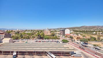 Uma rodoviária com vários ônibus, um estacionamento e vista para um horizonte urbano com edifícios e colinas.