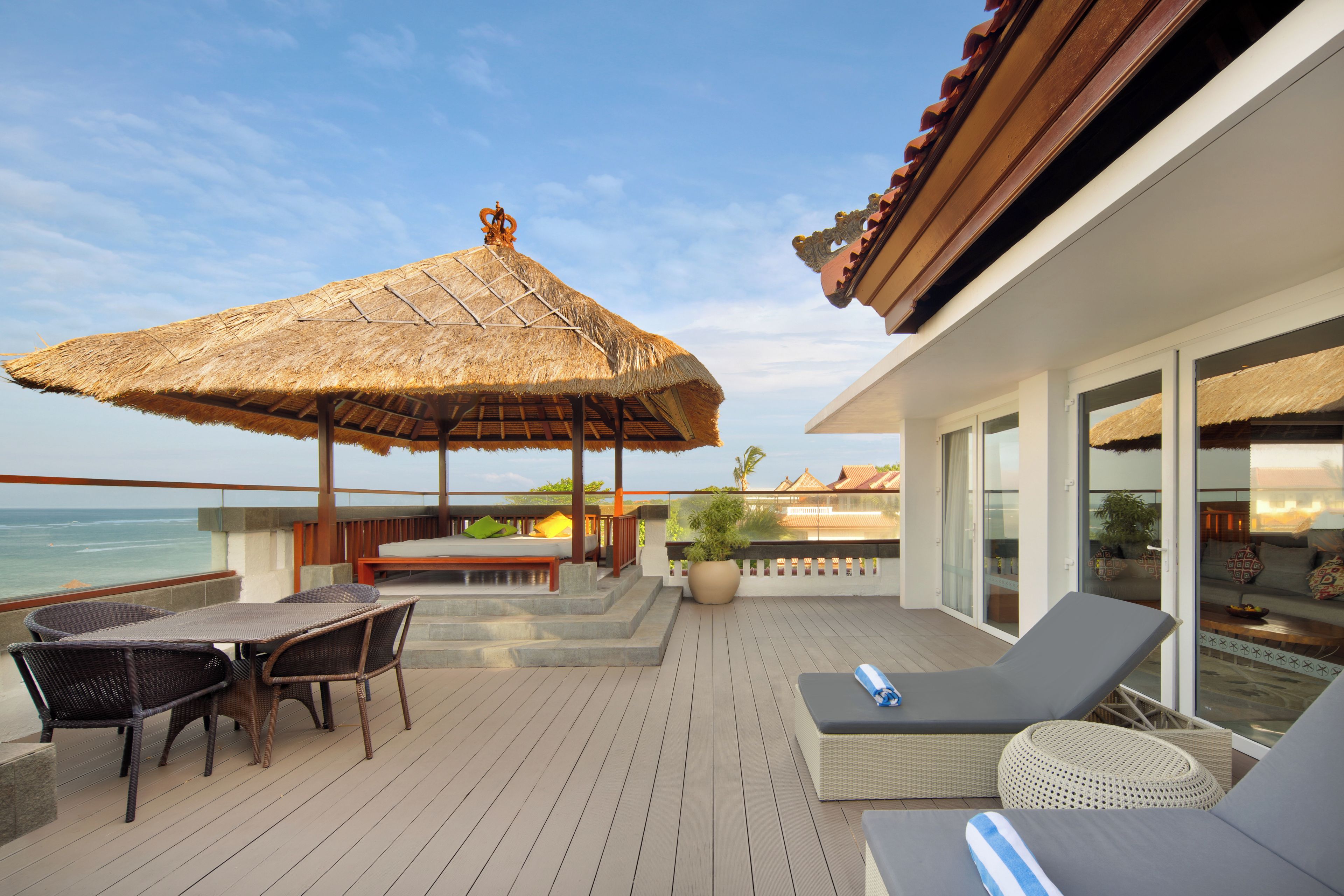 Um deck com um guarda-sol de palha, móveis de vime e vista para o mar.