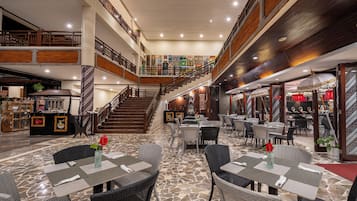 Um hall de hotel amplo em vários níveis, com escadaria, área de refeições e bar.