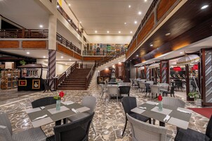 Um hall de hotel amplo em vários níveis, com escadaria, área de refeições e bar.