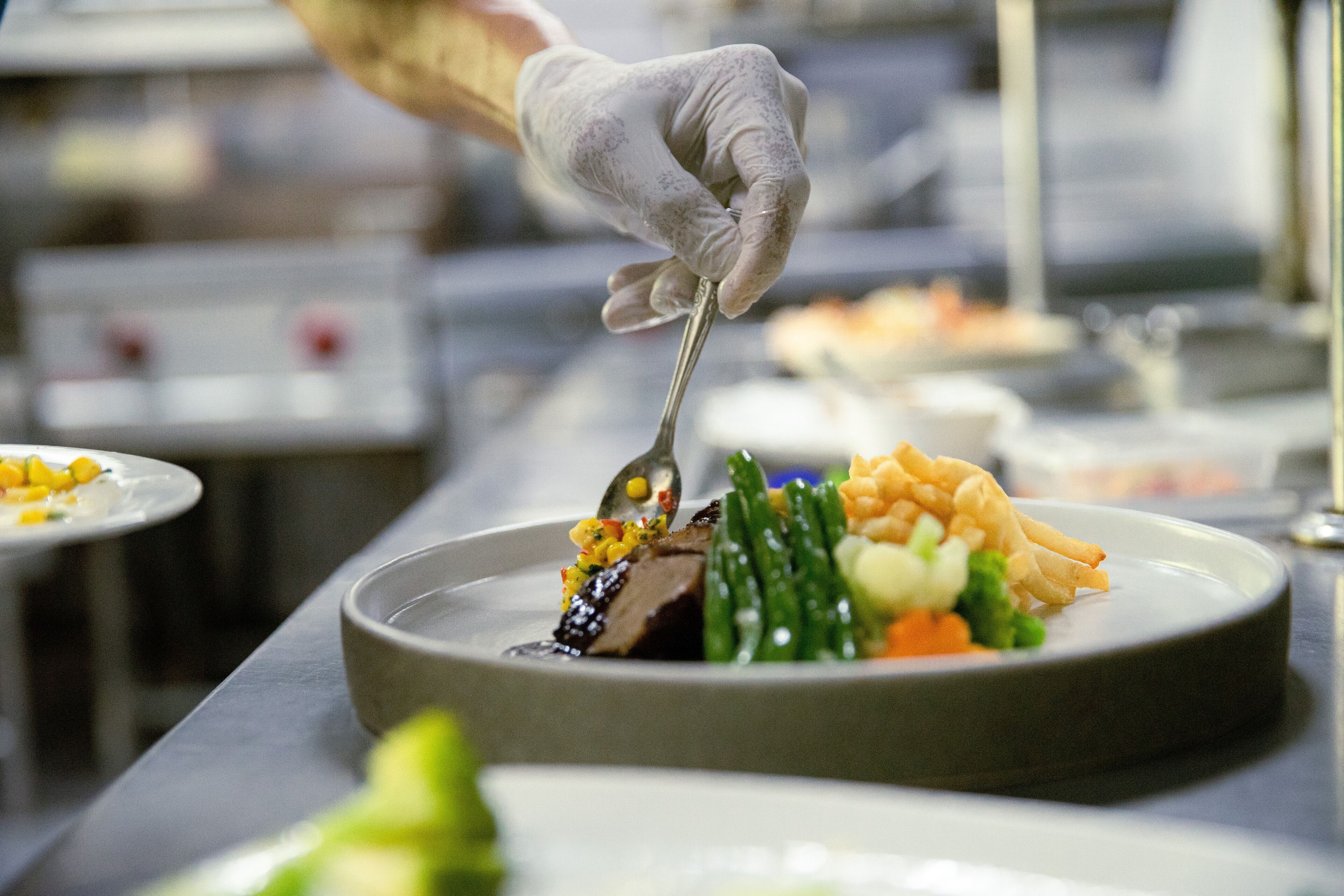 Mão de chef segurando uma colher, servindo comida em um prato.