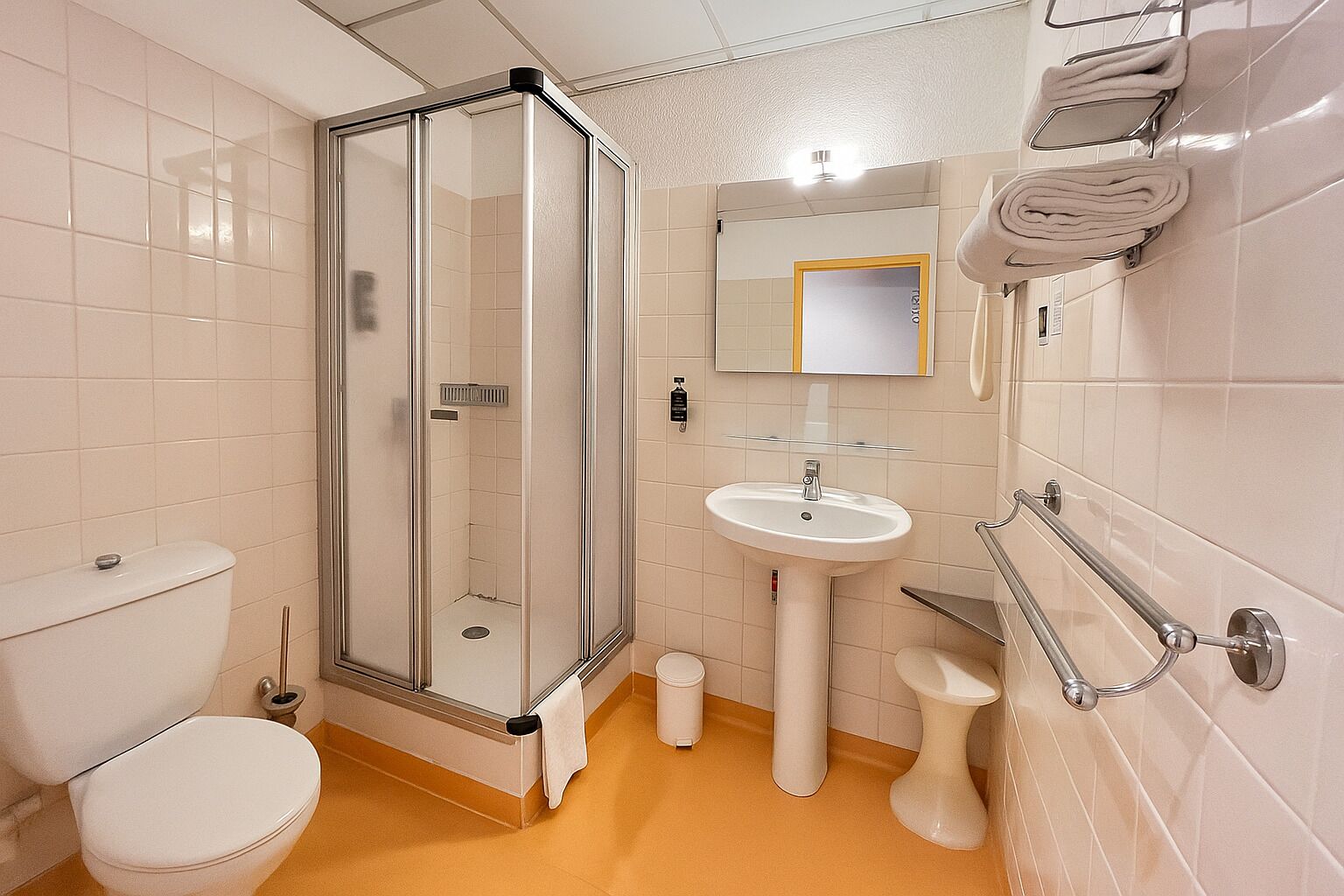 Casa de banho com chuveiro em cabine de vidro, lavatório branco, sanita e porta-toalhas.