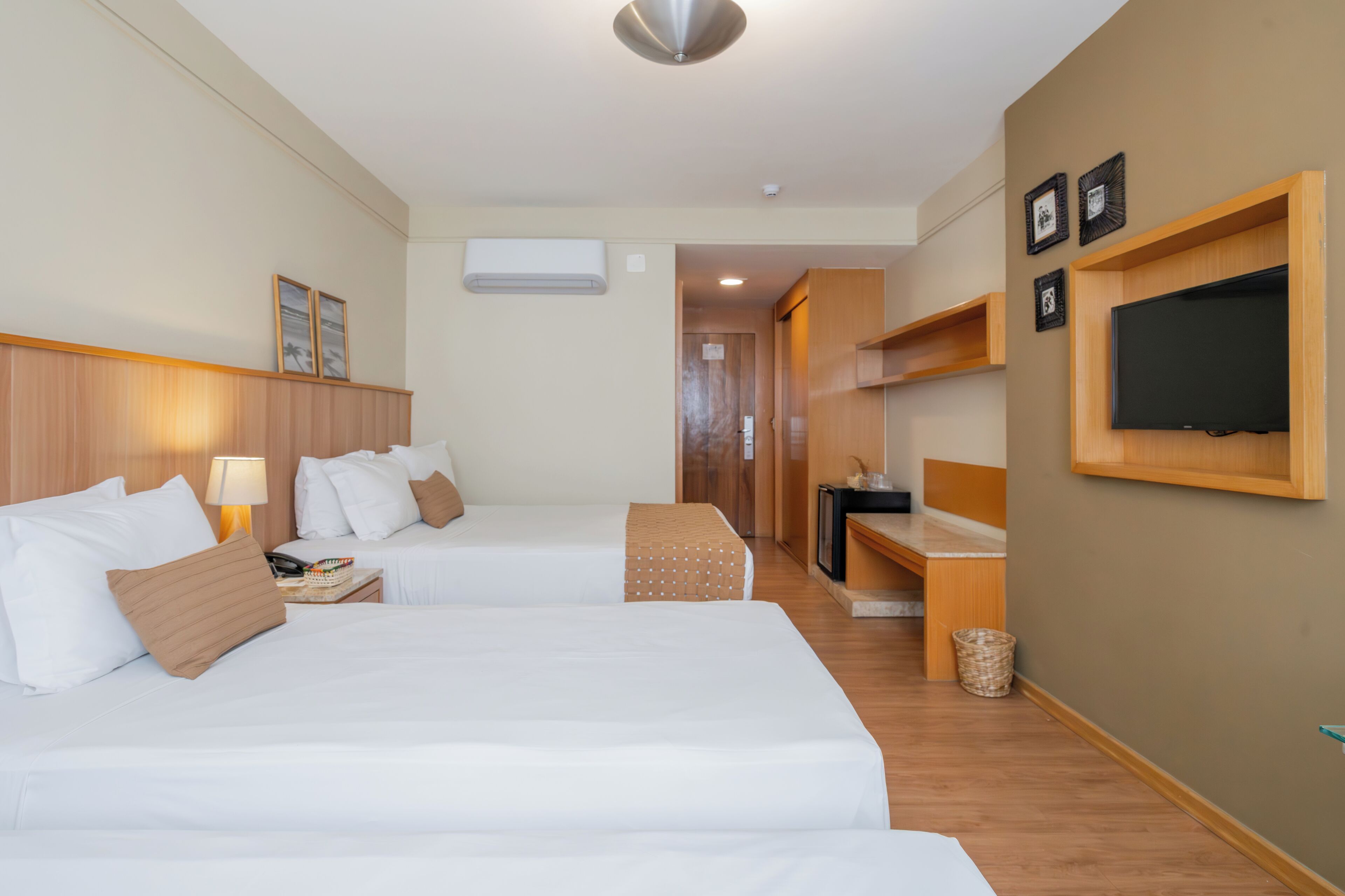 Quarto de hotel com duas camas, televisão, escrivaninha e um pequeno espaço para sentar.