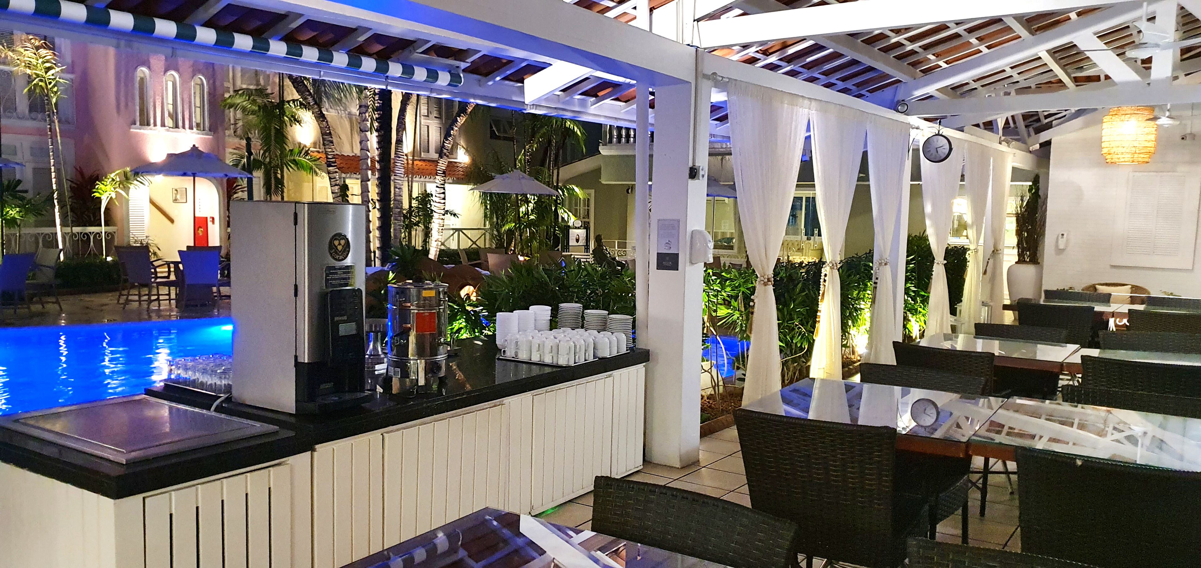 Uma área de bar junto à piscina, com balcão, cadeiras e mesas.
