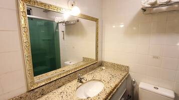 Casa de banho com lavatório bancada de granito, espelho com moldura dourada e sanita branca.