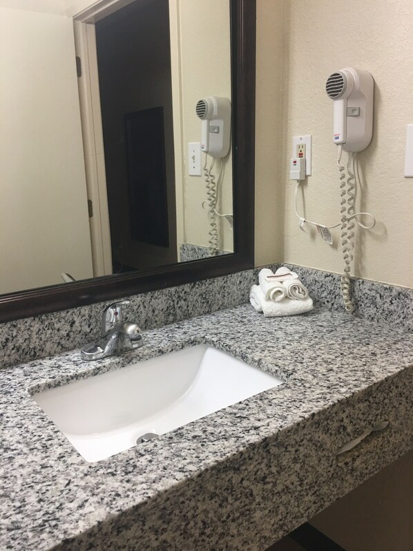 Casa de banho com lavatório de bancada em granito, espelho e secador de cabelo fixado na parede.