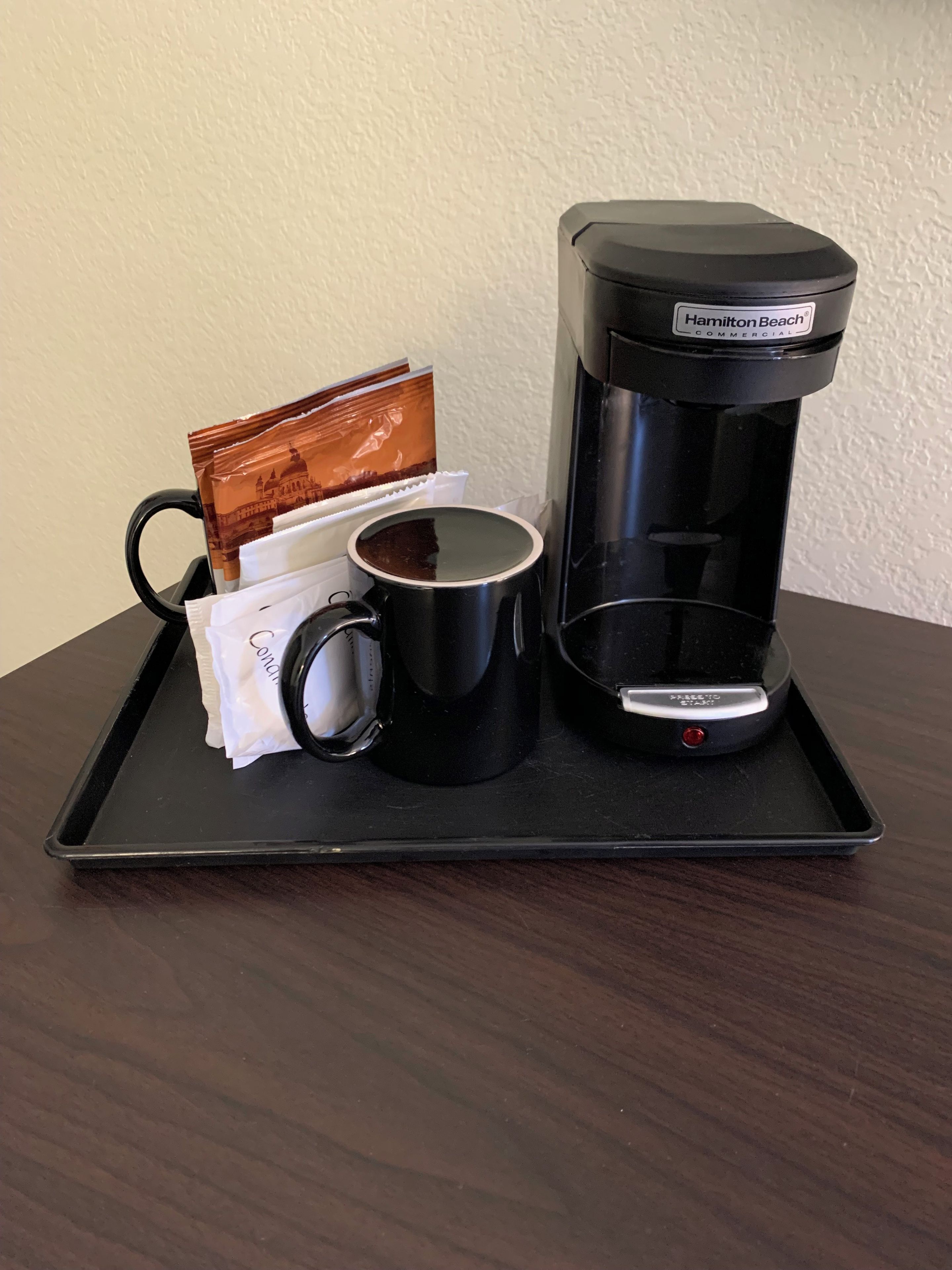 Uma cafeteira, uma caneca e um pacote de cápsulas de café em um tabuleiro.