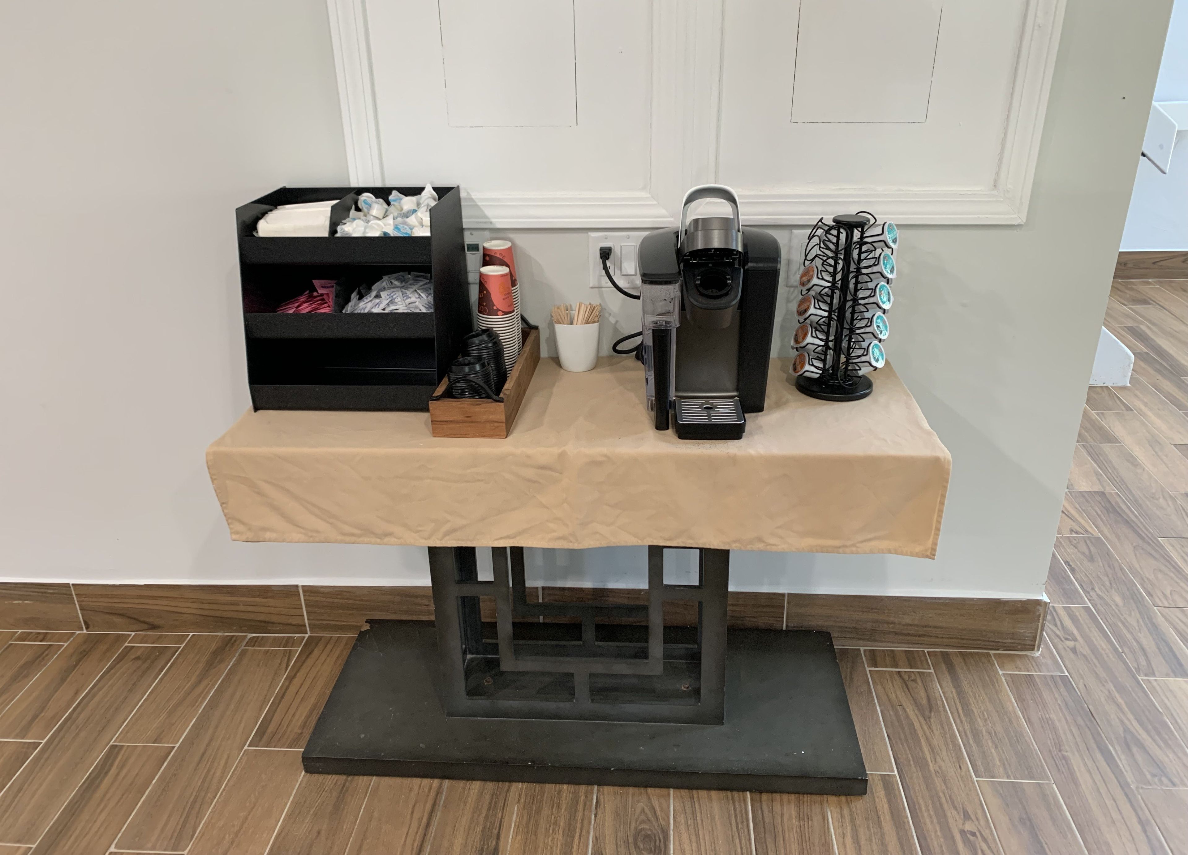 Cantinho do café com máquina de café, xícaras e bandeja com copos descartáveis.