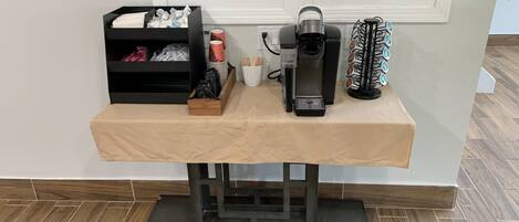 Cantinho do café com máquina de café, xícaras e bandeja com copos descartáveis.